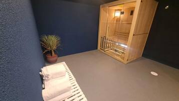 Uma área de spa com sauna de madeira, uma pequena planta em vaso e um porta-toalhas branco.