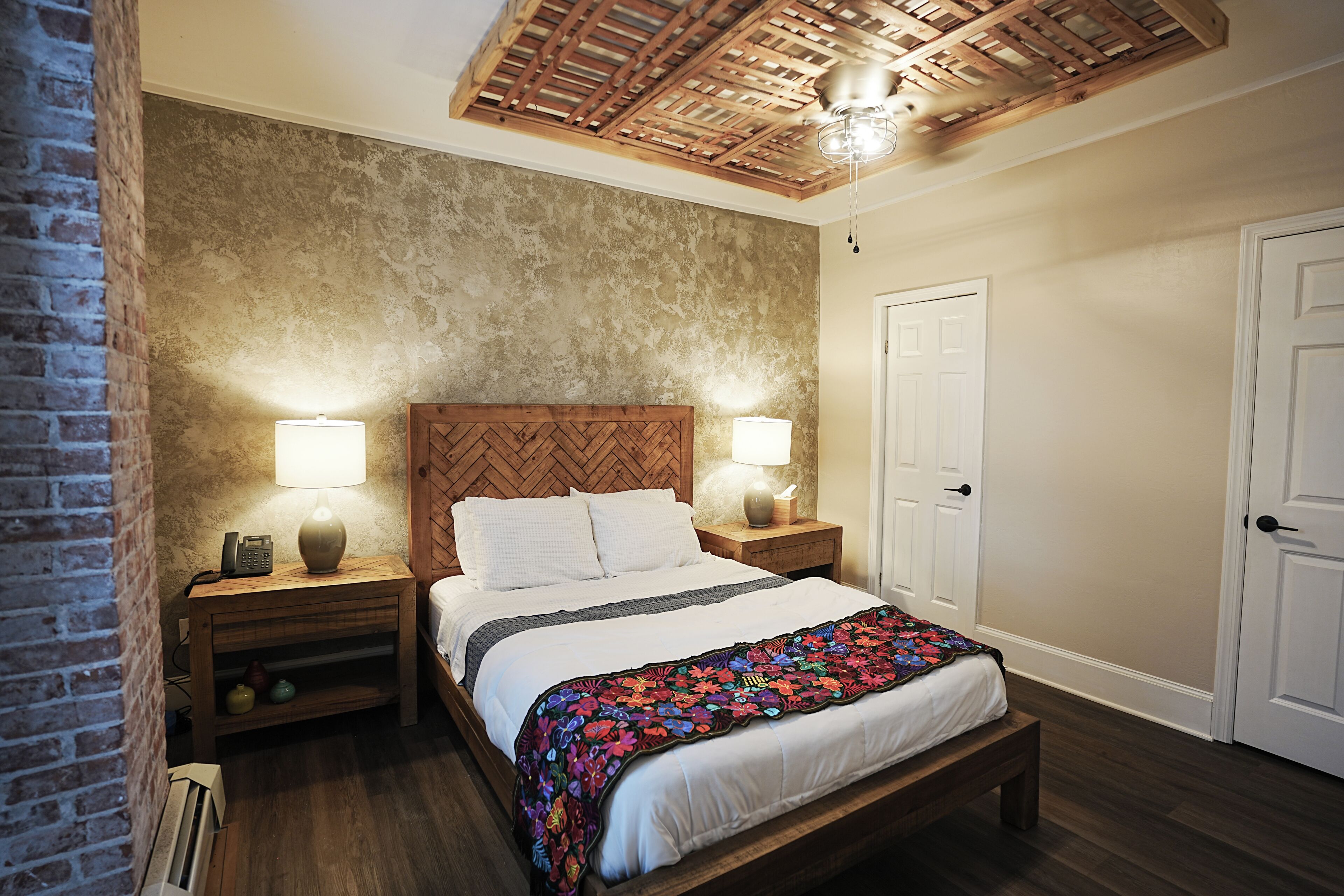 Quarto com cabeceira de madeira, cama com roupa de cama branca, duas luminárias de cabeceira, um banco no pé da cama e teto de madeira.