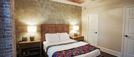 Quarto com cabeceira de madeira, cama com roupa de cama branca, duas luminárias de cabeceira, um banco no pé da cama e teto de madeira.
