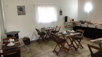 Uma área de refeições com mesas e cadeiras, uma janela com cortinas e um balcão com eletrodomésticos de cozinha.