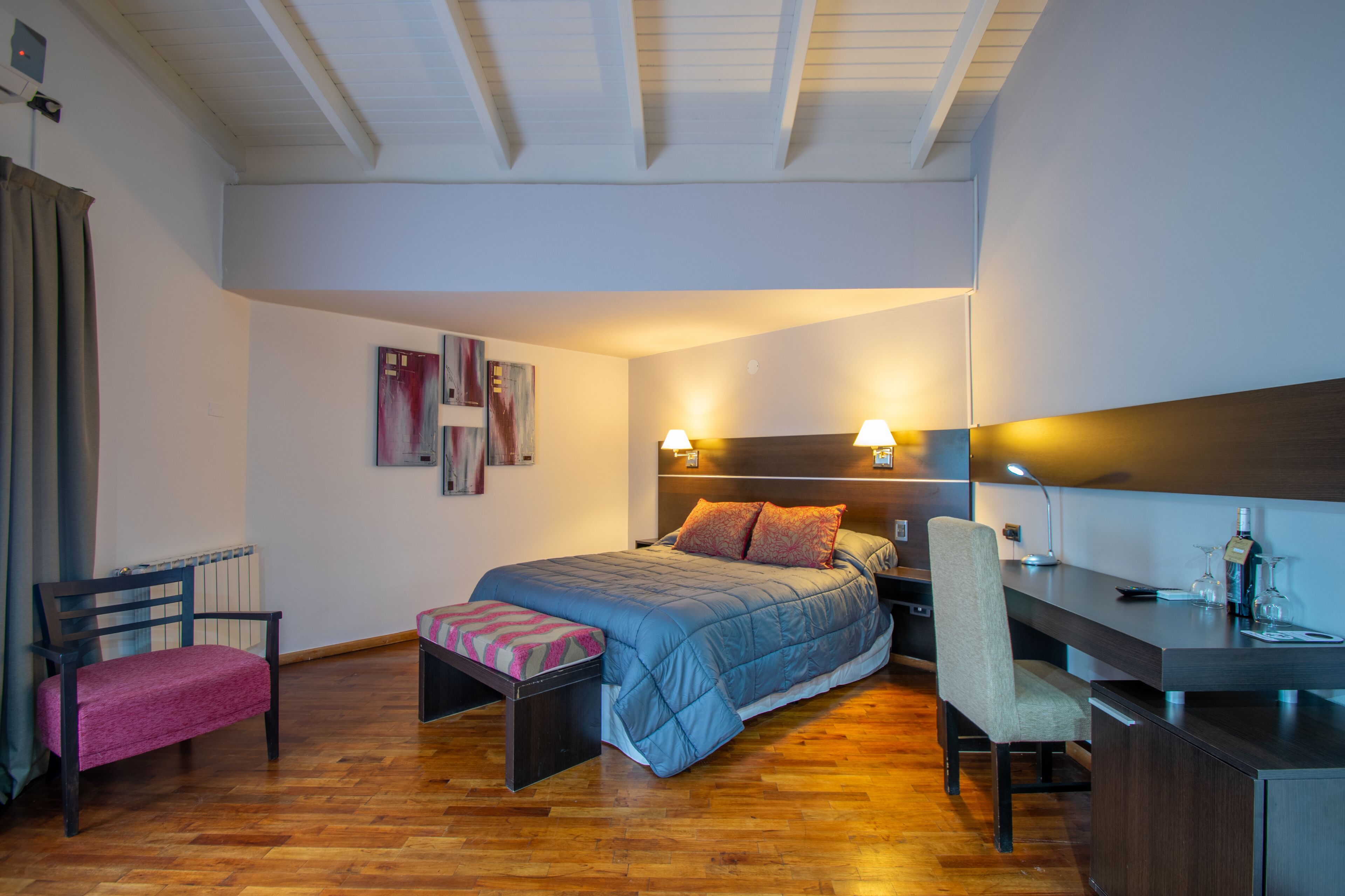 Quarto com cama, mesas de cabeceira, escrivaninha, cadeira, radiador e obra de arte na parede.