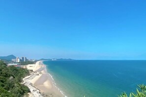 Vista costeira com praia, oceano e edifícios ao longe.