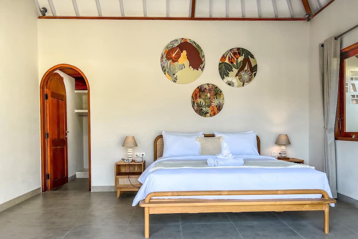 Quarto com cama de madeira, duas mesas de cabeceira e uma parede com três peças decorativas circulares.