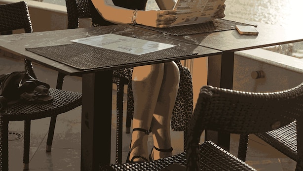 Uma mulher sentada à mesa com um menu, com vista para um corpo de água.