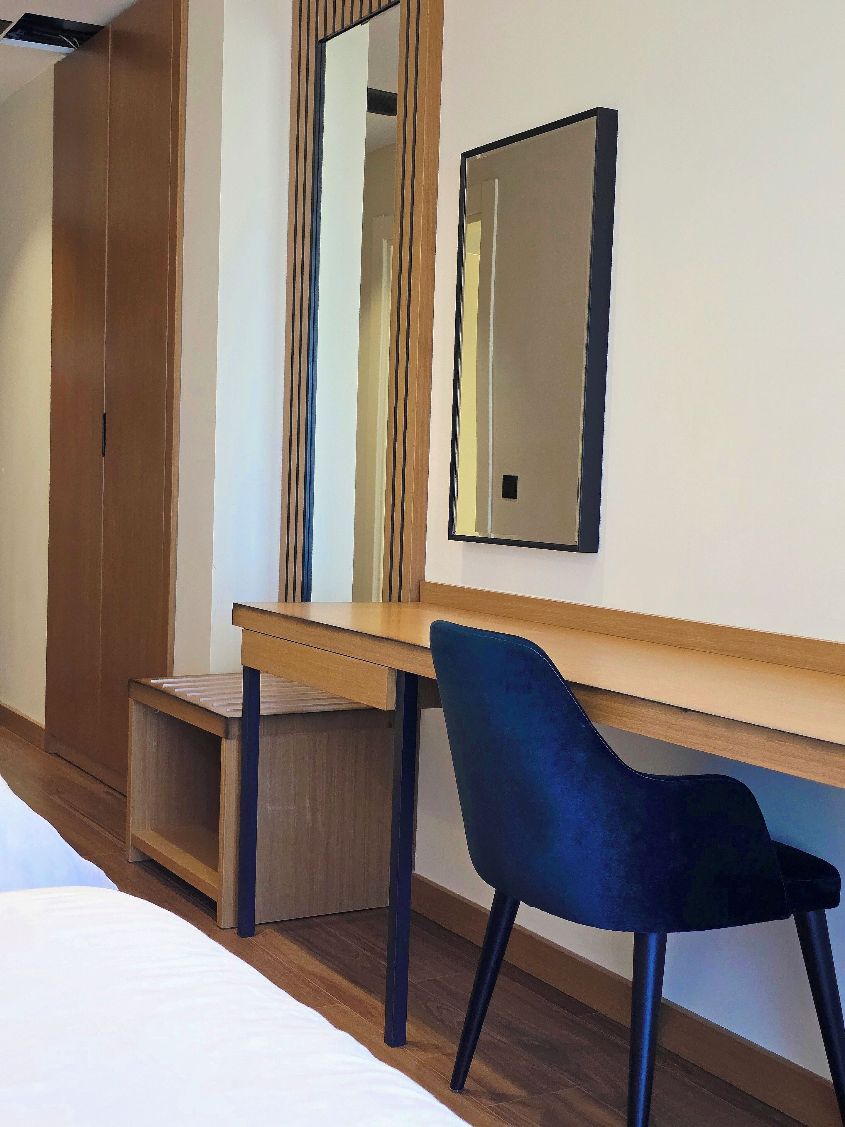 Quarto de hotel com escrivaninha de madeira, cadeira azul, cama e guarda-roupa.