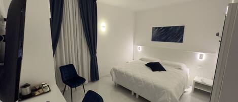 Quarto de hotel moderno com uma cama, uma escrivaninha com controle remoto, uma cadeira e um espelho grande.