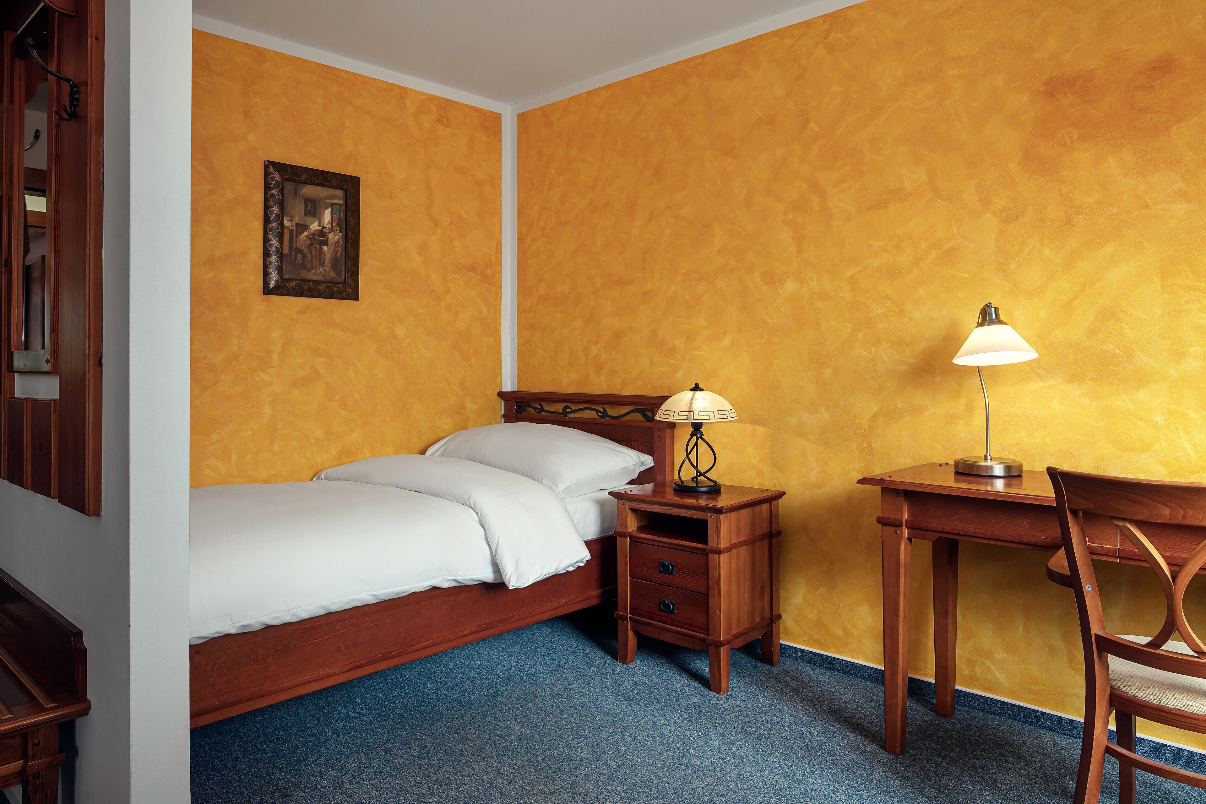 Quarto de hotel com cama, uma escrivaninha iluminada por um abajur e uma cadeira.