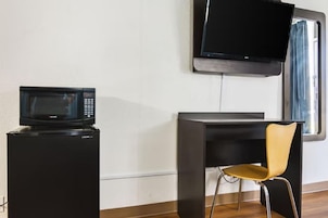 Uma cozinha compacta com micro-ondas, um frigorífico pequeno, uma televisão de ecrã plano na parede e uma cadeira moderna.