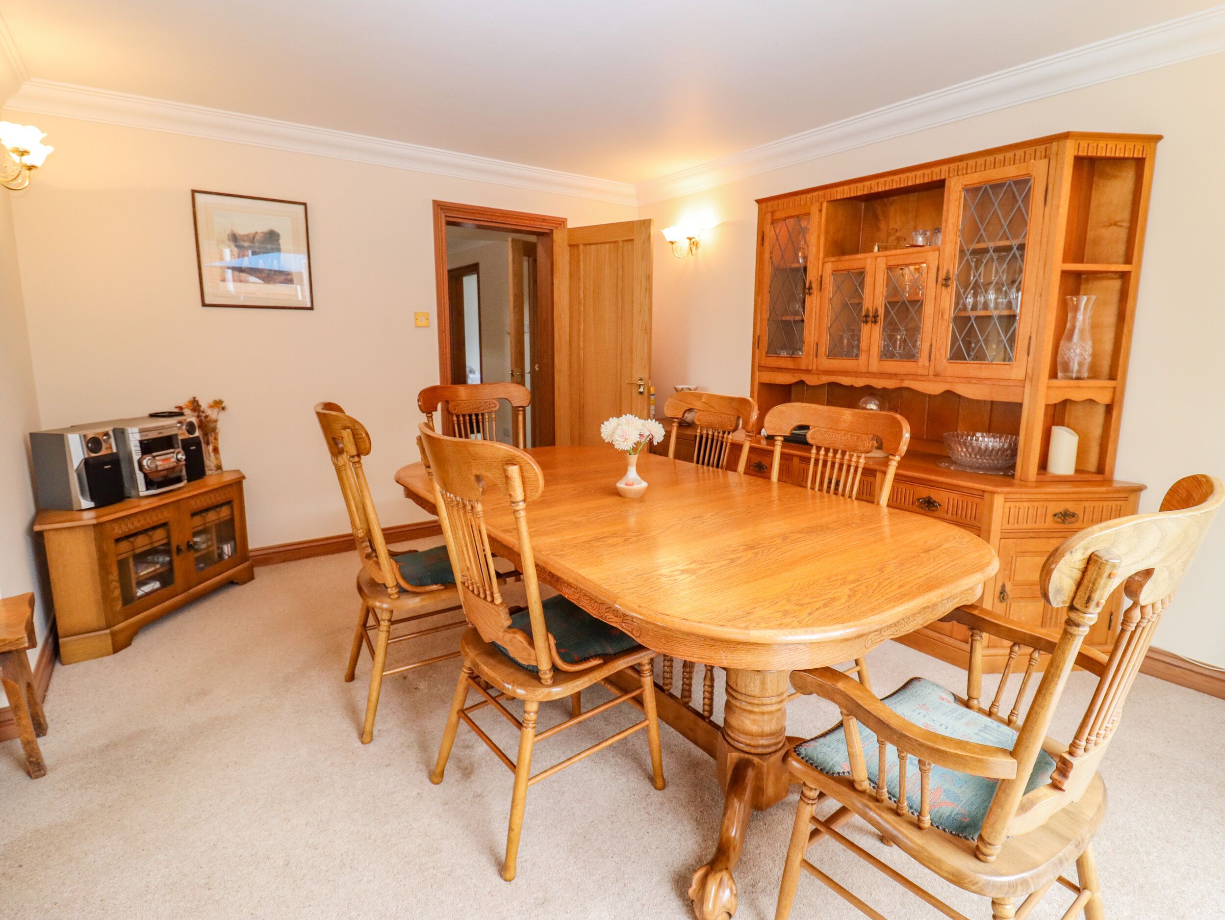 Uma sala de jantar com mesa e cadeiras de madeira, um armário com portas de vidro e um quadro na parede.
