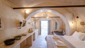 Quarto amplo com uma cama grande, mesa de cabeceira e vista para uma varanda por uma porta em arco.