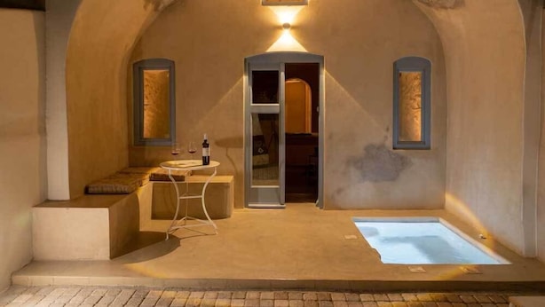 Uma área de spa com arco de pedra, um espaço de estar pequeno, mesa com uma garrafa e ofurô.