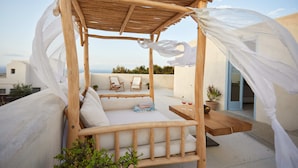 Uma cama de dossel de madeira com roupa de cama branca, uma mesa de madeira com duas taças de vinho e duas cadeiras.