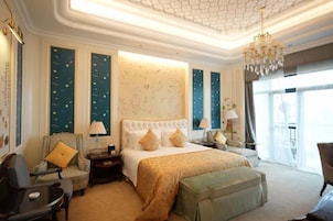 Quarto de hotel espaçoso com uma cama grande, área de estar com uma cadeira e mesa, e varanda com vista.