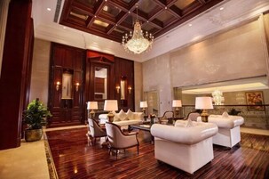 Um hall espaçoso com um imponente candelabro, assentos confortáveis e um espelho grande refletindo o ambiente.