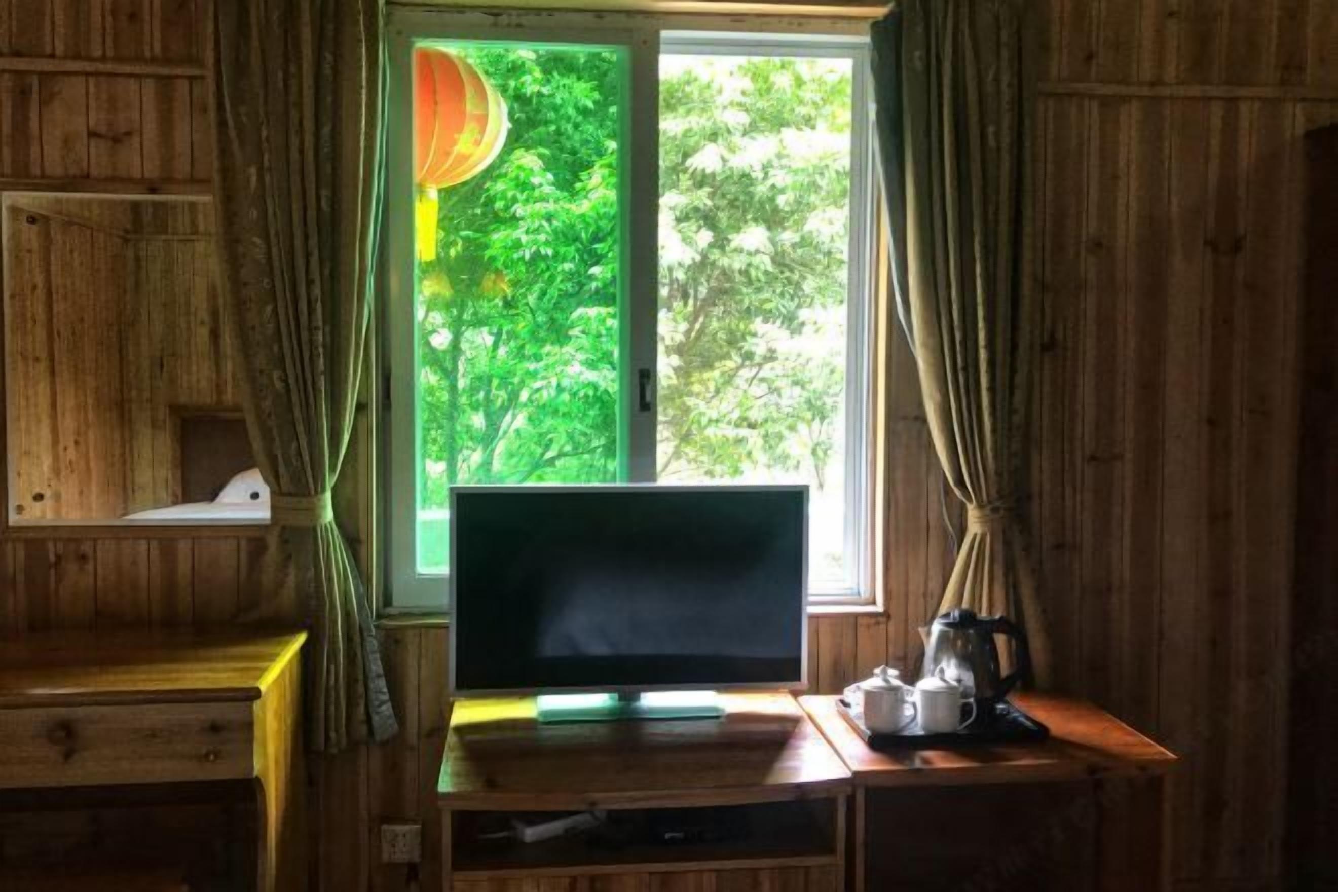 Um quarto de madeira com uma televisão sobre um suporte de madeira, uma janela com cortinas e uma cafeteira no parapeito.