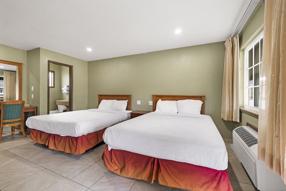 Quarto de hotel com duas camas, uma escrivaninha e uma janela com cortinas.