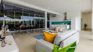Uma sala de estar moderna com um sofá cinzento, almofada amarela e uma janela grande com vista para uma varanda.