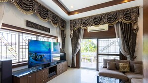 Uma sala de estar com uma grande televisão de tela plana, armários de madeira escura, um sofá bege e cortinas decorativas.