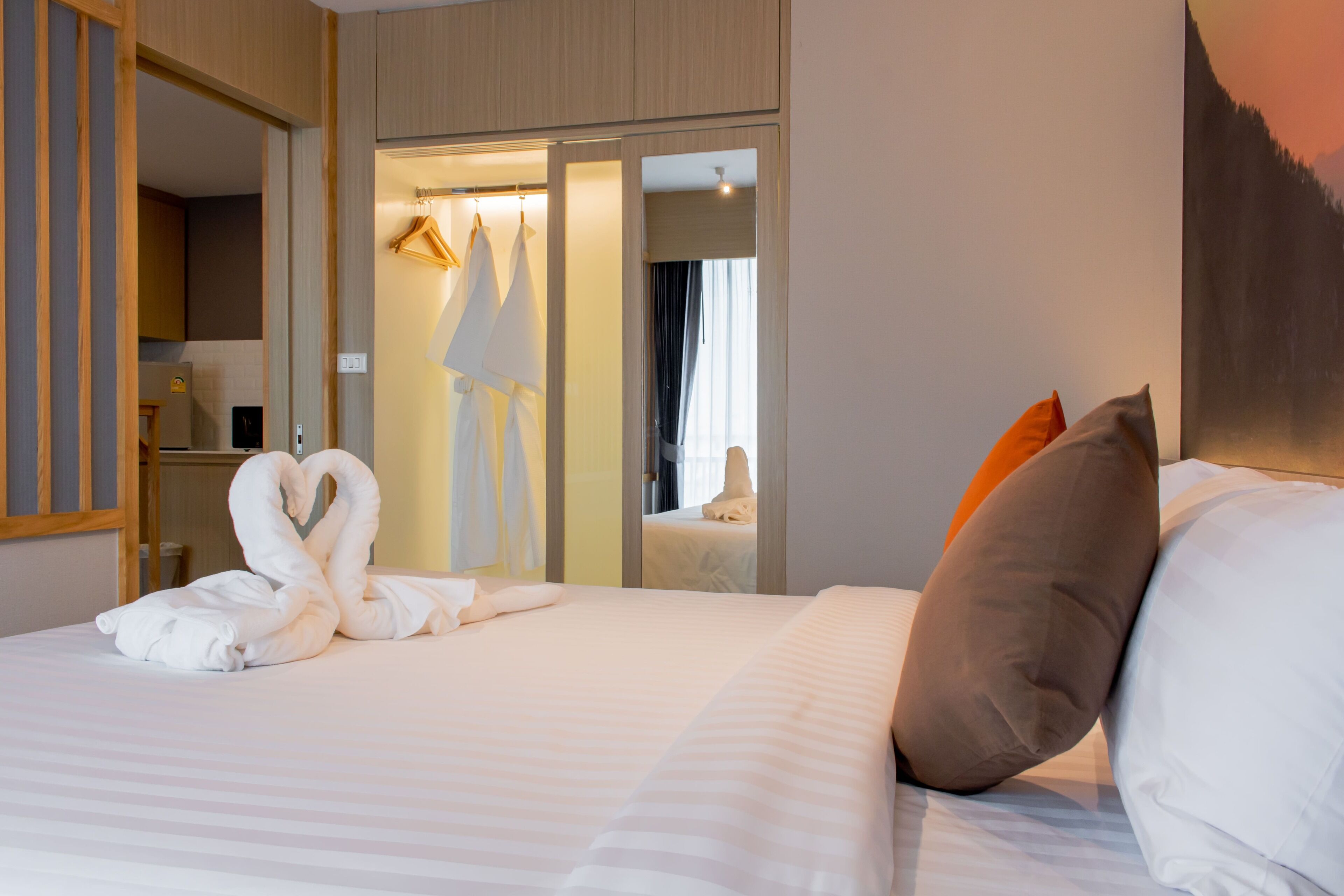 Quarto de hotel com uma cama bem arrumada, um espelho e um guarda-roupa cheio de roupas.