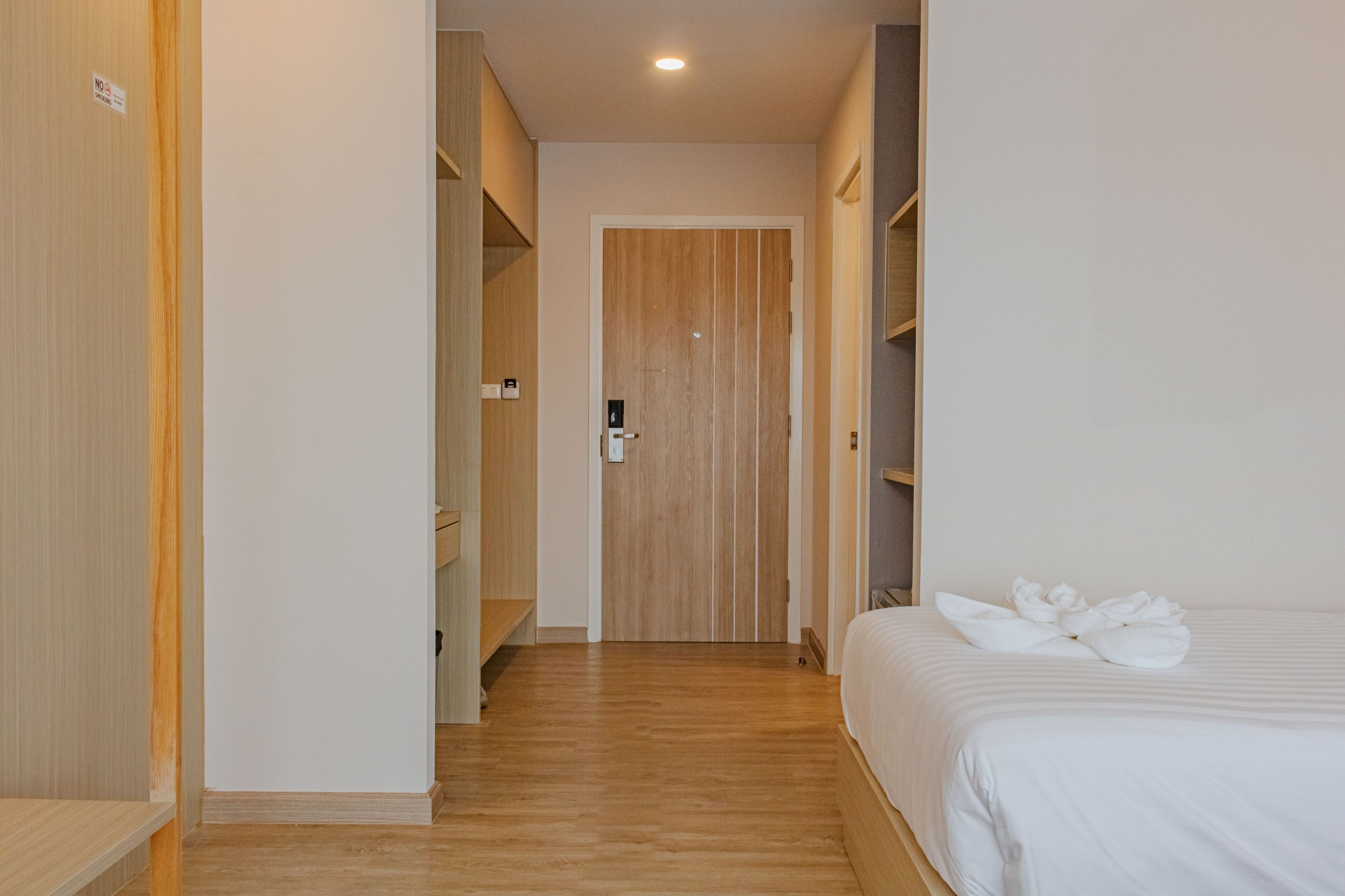 Quarto de hotel com piso de madeira, uma cama com roupa de cama branca e um guarda-roupa de madeira.