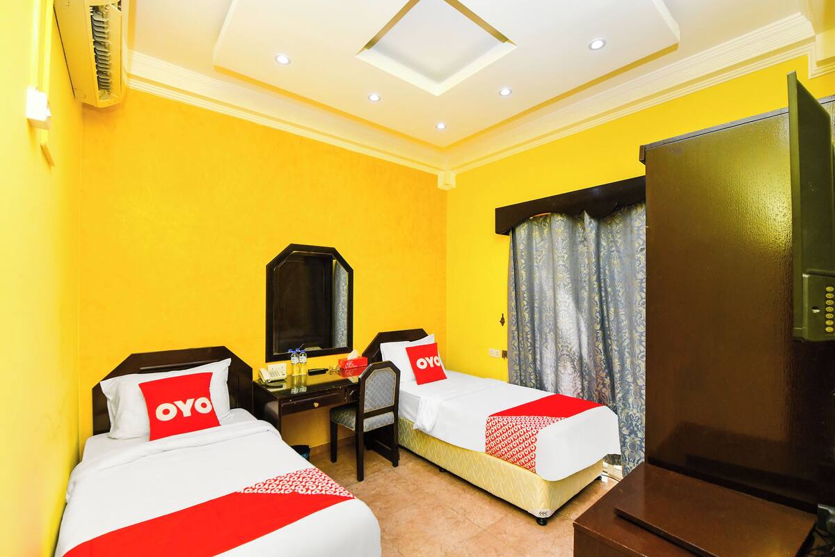 Quarto de hotel com duas camas, uma escrivaninha, uma cadeira, uma televisão e um espelho.