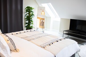 Quarto moderno com uma cama grande, uma televisão, um claraboia e uma planta em vaso.