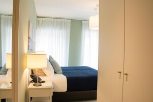 Quarto de hotel com cama, mesas de cabeceira, telefone e guarda-roupa.