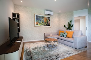 Uma sala de estar com sofá, mesa de centro, televisão e um quadro na parede.