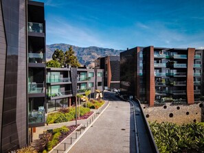 Um edifício moderno com várias varandas, um caminho pavimentado e montanhas ao fundo.