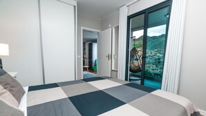 Quarto de hotel com uma cama grande, porta de correr de vidro que dá para uma varanda com vista para a cidade.