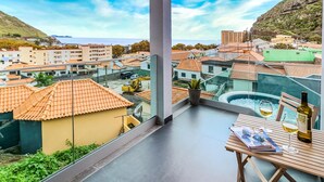Varanda com vista para uma cidade costeira, hidromassagem e mesa com garrafa e copos.