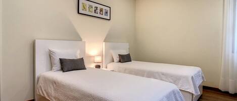 Quarto de hotel com duas camas de solteiro, uma fotografia emoldurada na parede e piso de madeira.