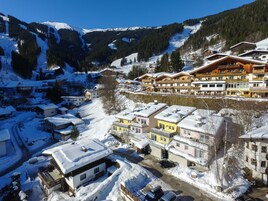 Uma aldeia montanhosa coberta de neve, com edifícios de madeira tradicionais e uma estância de esqui ao fundo.