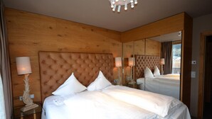 Quarto de hotel com uma cama grande, paredes de painel de madeira, um espelho e um candelabro.
