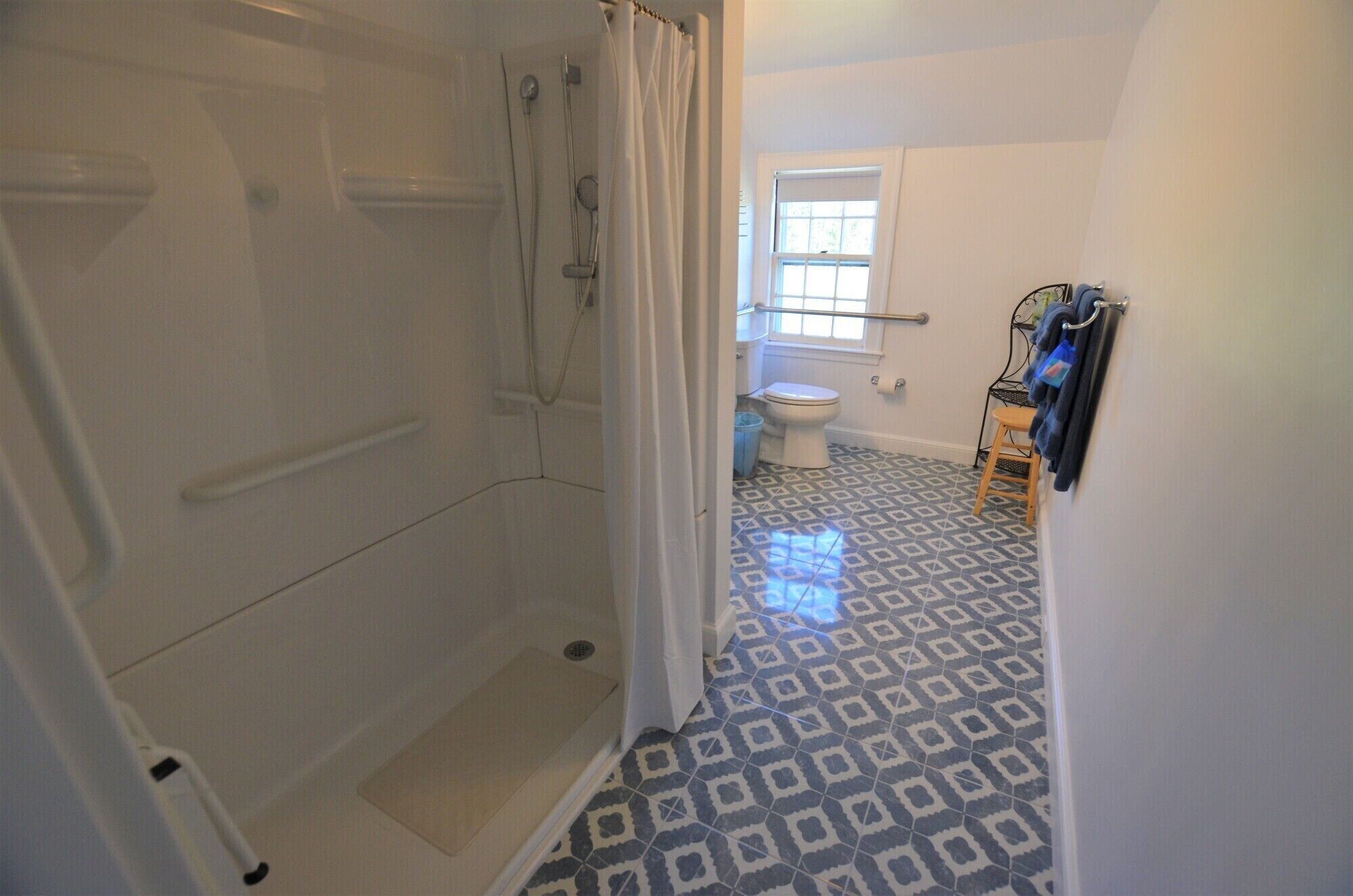 Casa de banho com chuveiro, sanita e pavimento com azulejos estampados.