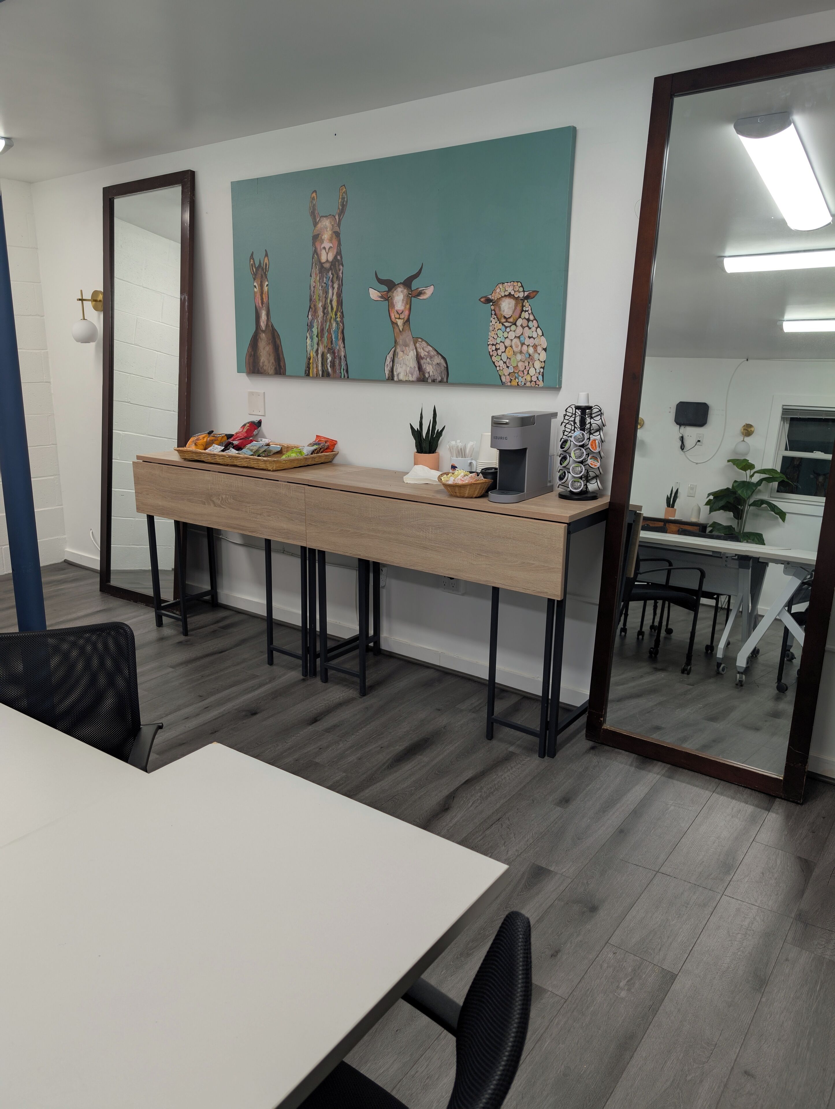 Um espaço de escritório moderno com uma mesa de madeira comprida, uma máquina de café e um espelho fixado na parede.