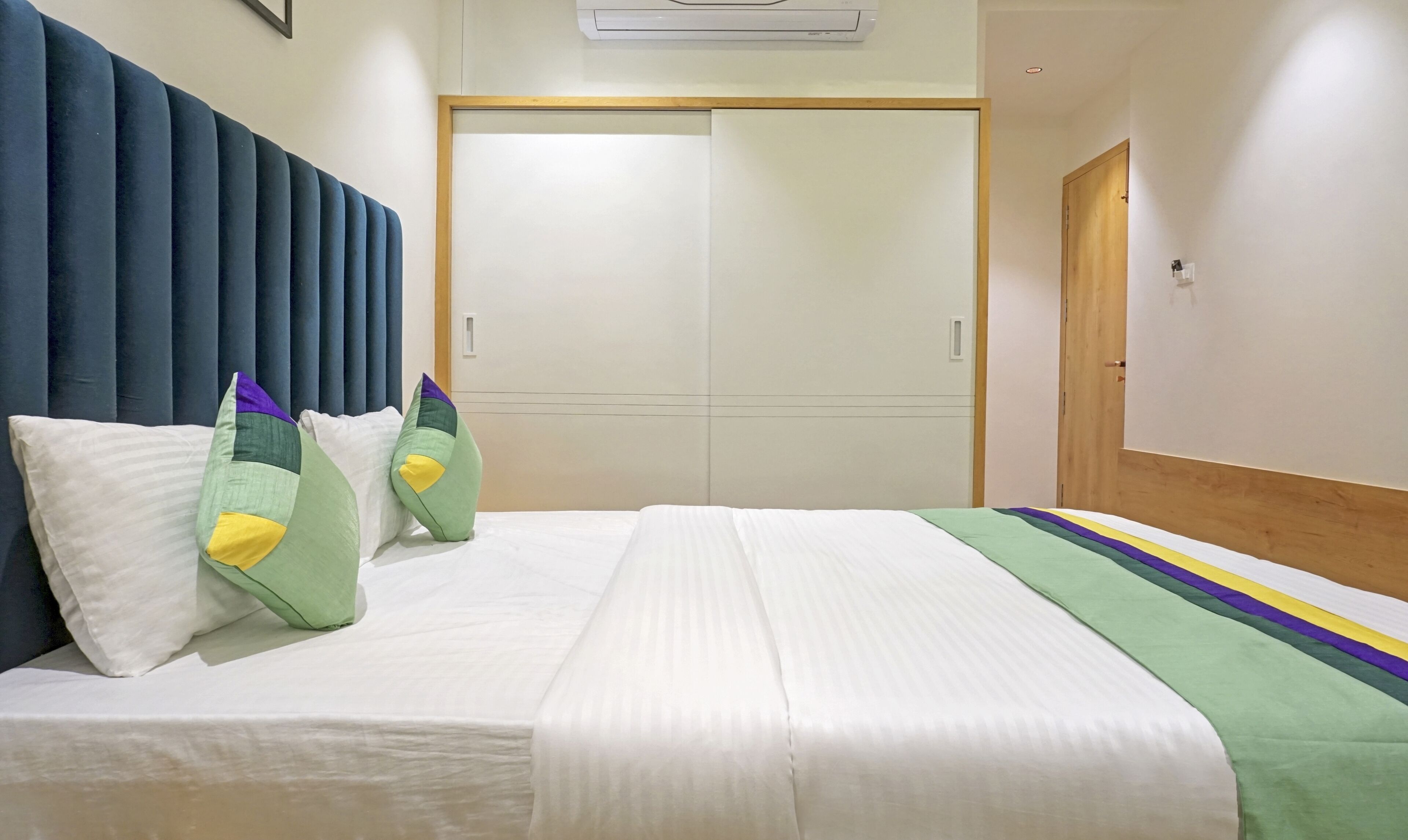 Quarto de hotel com uma cama, cabeceira azul e porta de madeira.