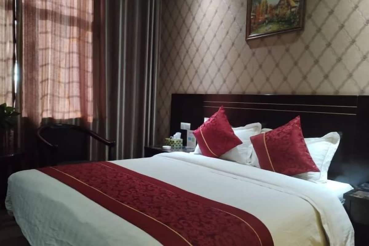 Quarto de hotel com uma cama grande, cabeceira, mesa de cabeceira, uma cadeira e um quadro na parede.