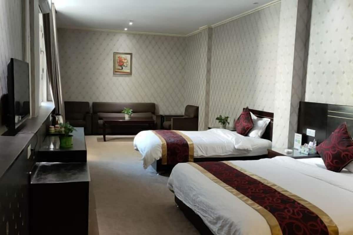 Quarto de hotel com duas camas, um sofá, uma televisão e uma pequena mesa com uma planta.