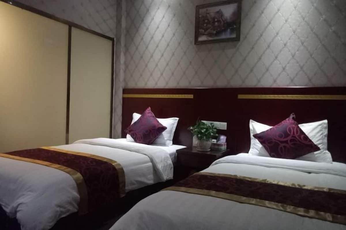 Quarto de hotel com duas camas, uma mesa de cabeceira com uma planta e um quadro na parede.