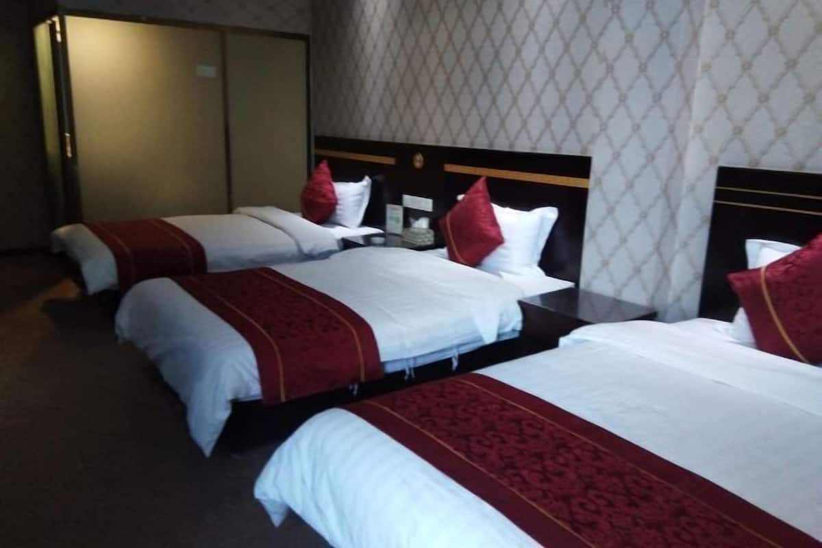 Quarto de hotel com três camas, cada uma com roupa de cama branca e detalhes vermelhos, cabeceira de madeira e papel de parede estampado.