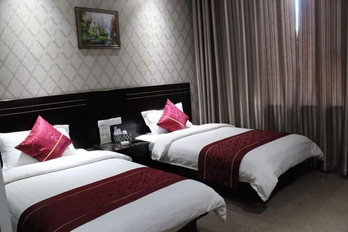 Quarto de hotel com duas camas, uma mesa de cabeceira, um quadro na parede e uma janela com cortinas.