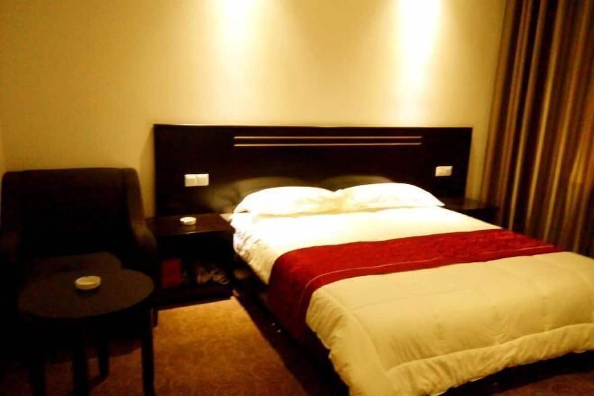 Quarto de hotel com uma cama, uma cadeira, uma mesinha e um criado-mudo.