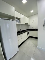 Uma cozinha compacta com armários brancos, bancada preta, geladeira branca e micro-ondas.