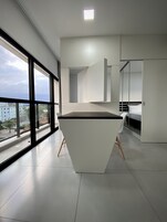 Quarto moderno e minimalista com uma grande janela, uma secretária branca e uma cama com divisória de vidro.