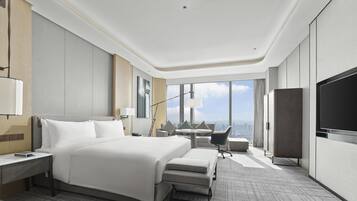 Quarto de hotel moderno com uma cama grande, escrivaninha, cadeira, televisão e vista para a cidade.