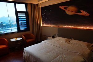 Quarto de hotel com uma grande janela, uma cama, uma pequena mesa redonda, duas poltronas e um mural na parede retratando um planeta com anéis.