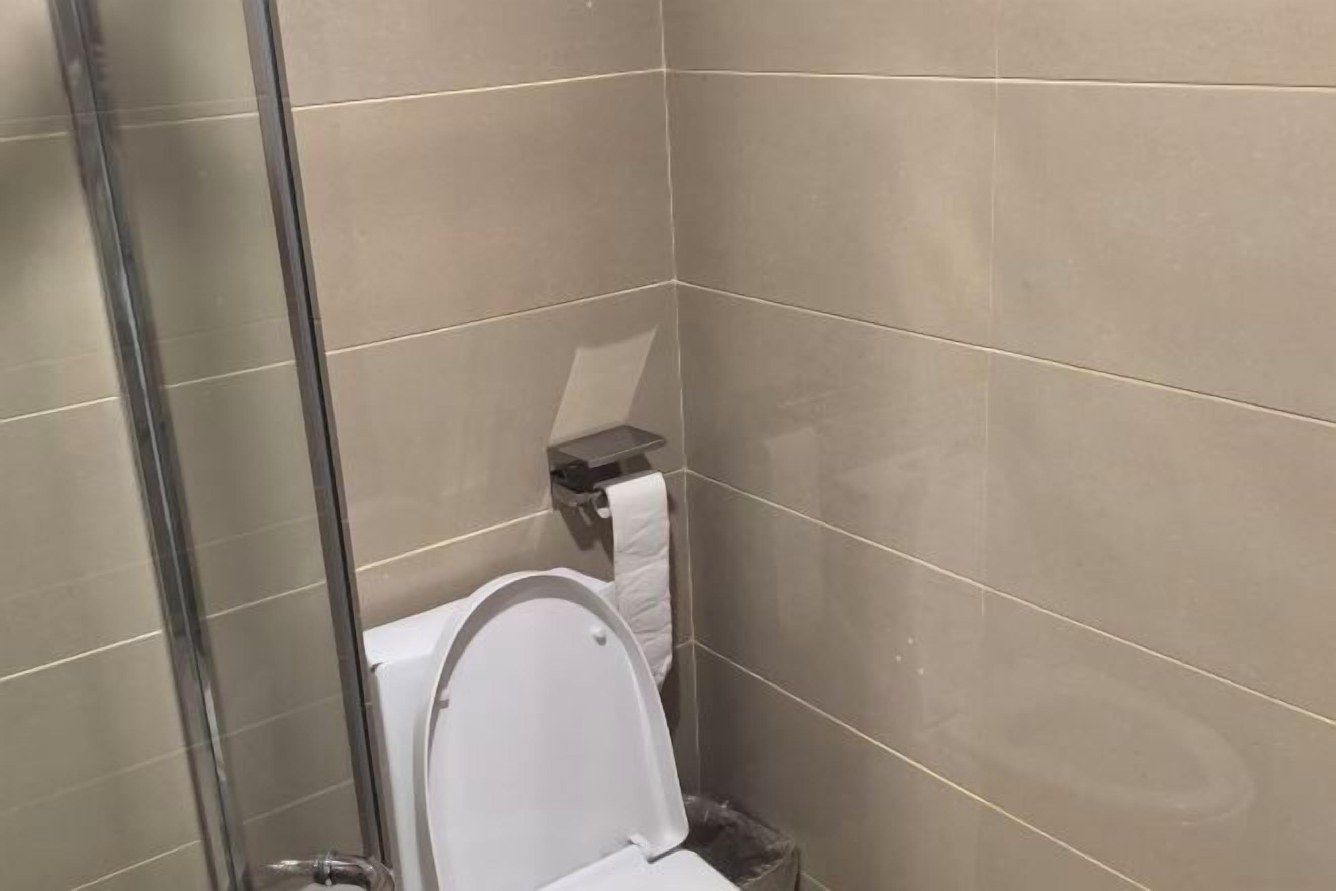 Um banheiro pequeno e fechado com vaso sanitário, lixeira e divisória de vidro.