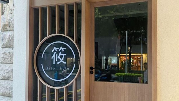 Placa de hotel com caracteres chineses e o nome 'Xiao Hotel' em uma porta de madeira.