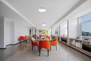 Uma sala de jantar moderna com uma mesa comprida, cadeiras laranjas e vista para a cidade.